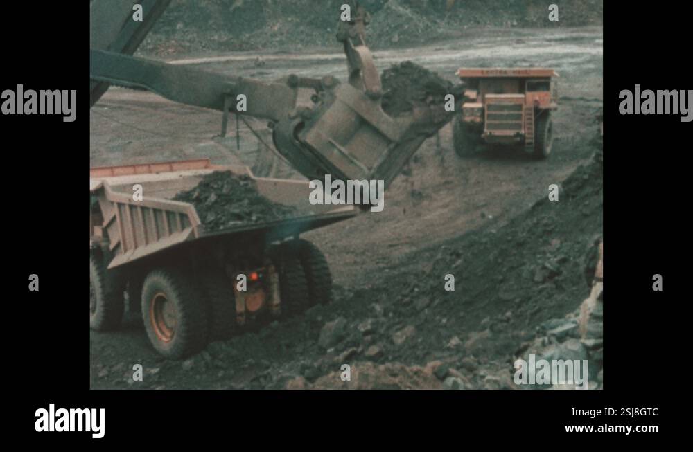 1980s: Machine digging rock, dumping rock into truck. Machine crushing ...