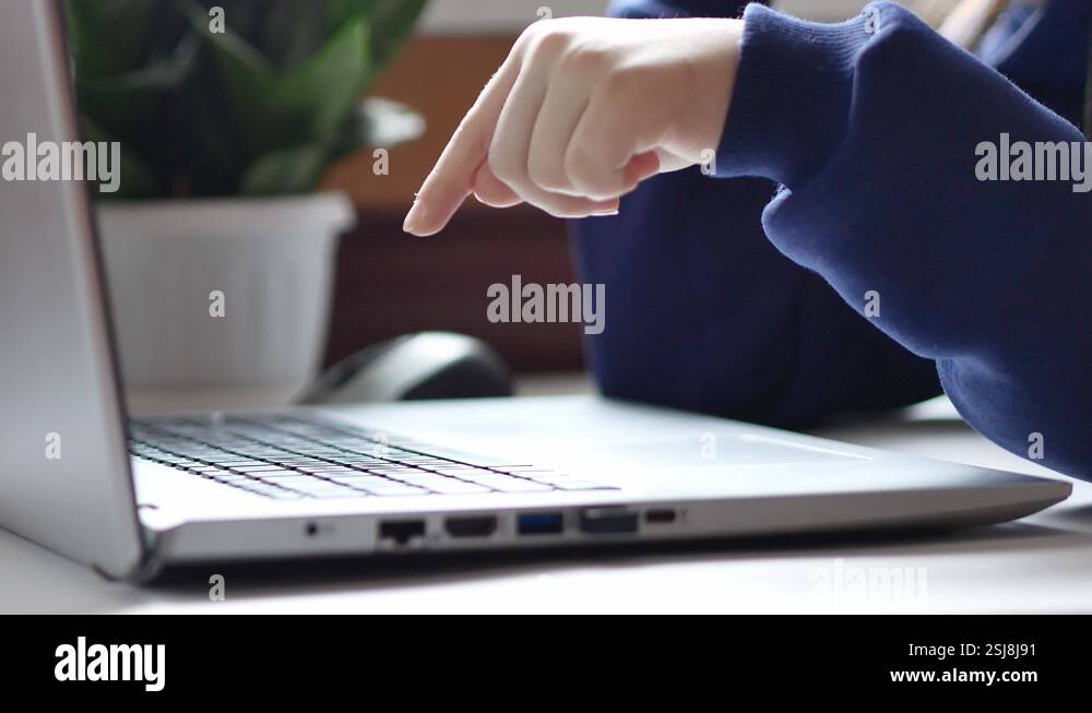 A child's hand in a blue jumper presses the button of the laptop ...