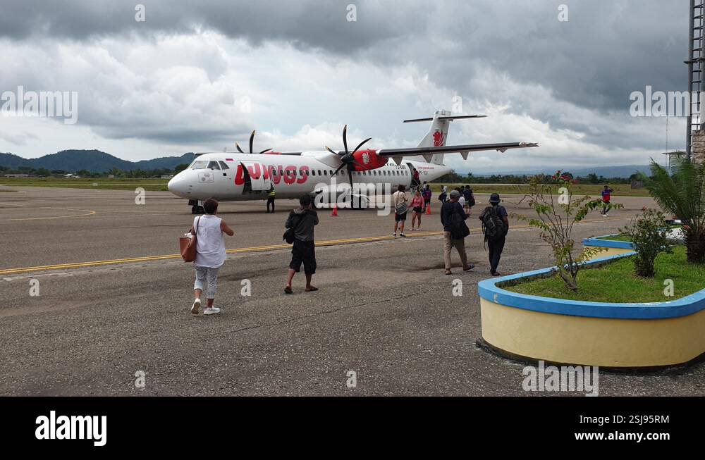 Passengers walking across the runway to board Wings Air airplane flight ...