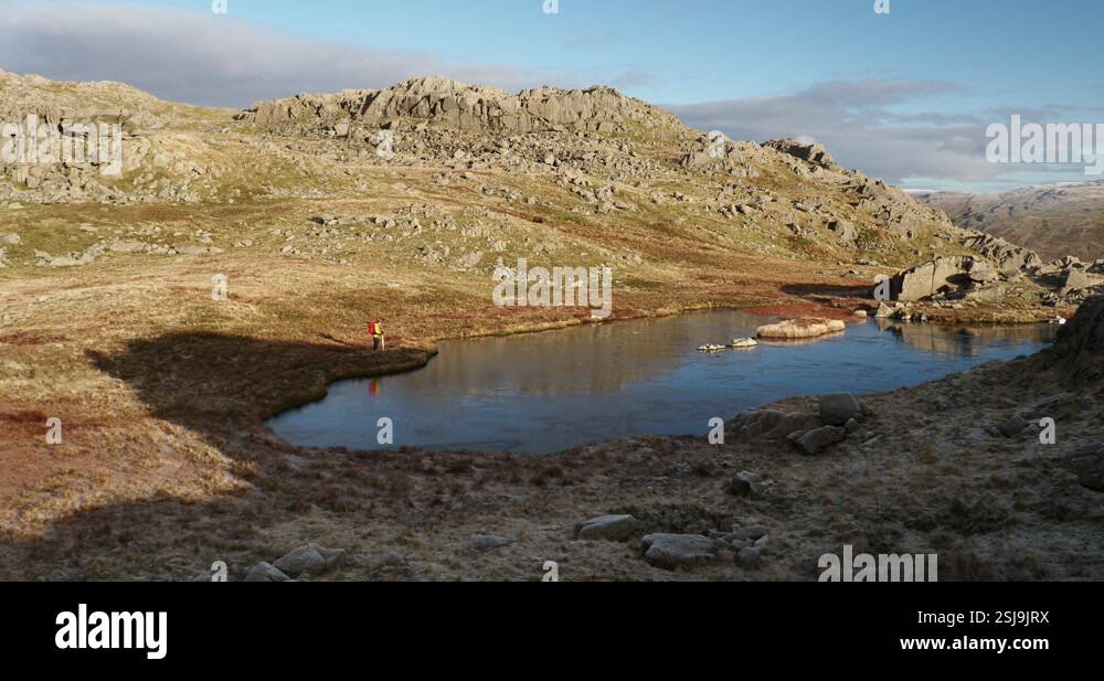 A hiker next to a frozen tarn on Glaramara, Lake District, UK Stock ...
