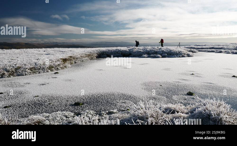 Hikers by a frozen tarn with rime ice on High Raise on a frosty morning ...