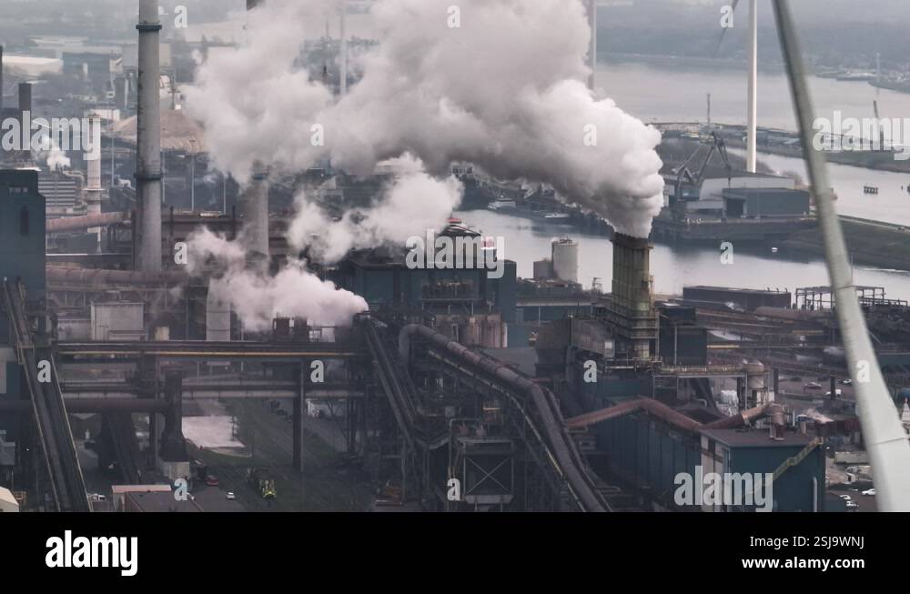 Aerial panning shot of Tata steel mill in the port of Ijmuden releasing ...