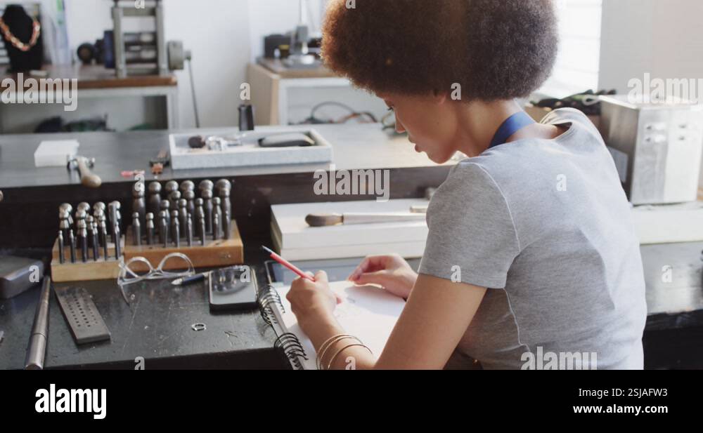 Biracial female worker drawing design of jewellery in workshop in slow ...