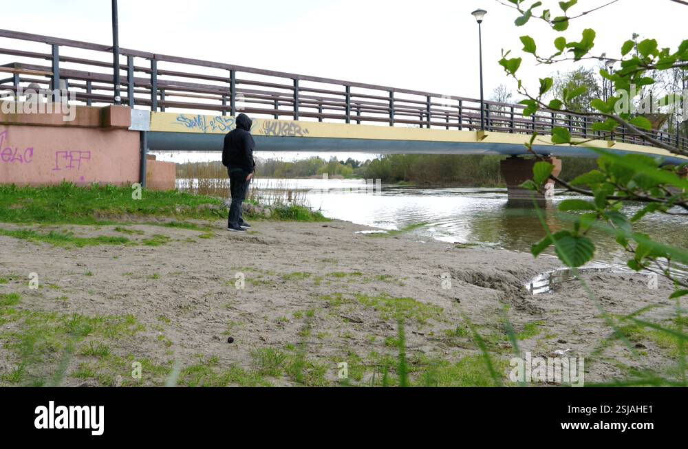 A man by the lake shore bridge is throwing stones into the water Stock ...