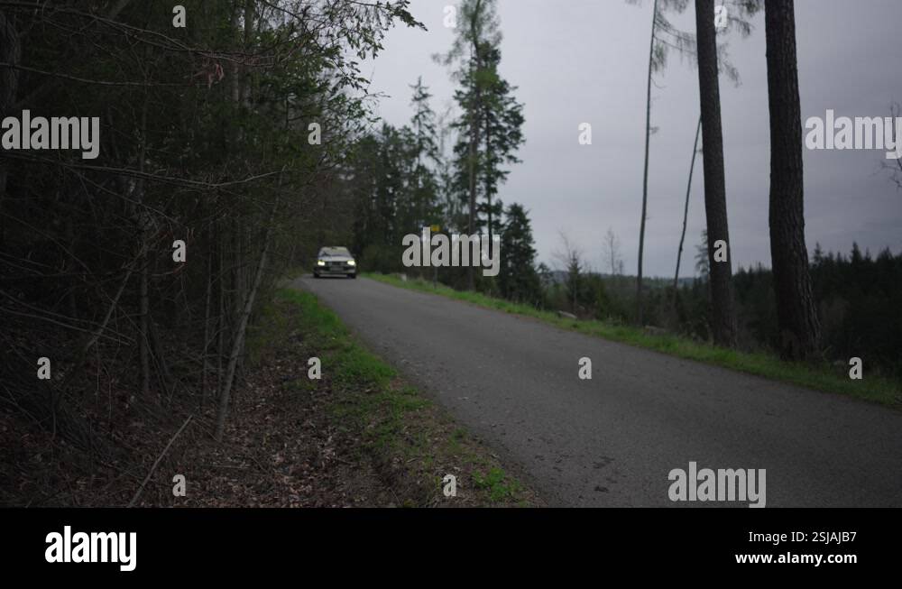 Camera follows vintage car speeding through narrow forest asphalt road ...