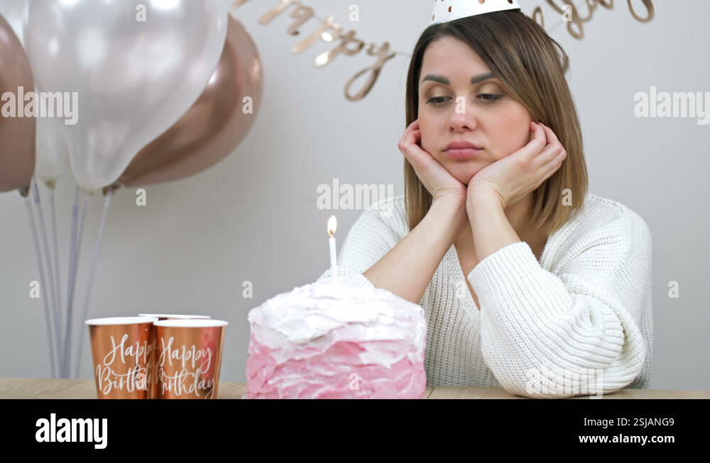 Sad birthday. Beautiful girl sits alone in front of a birthday cake ...