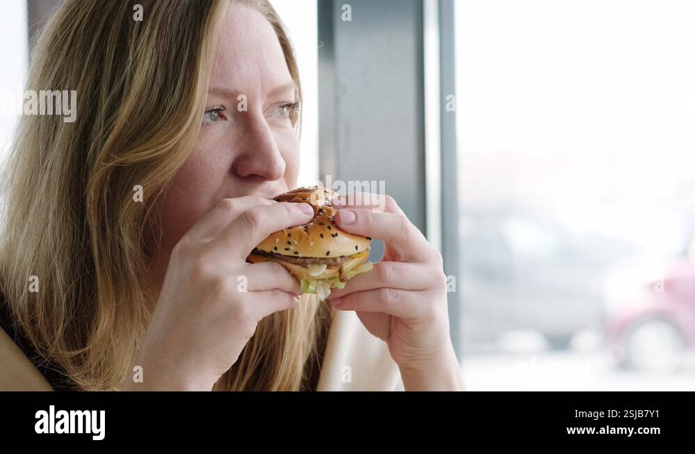 side view woman eating Big burger in fast food Restaurant, unhealthy ...