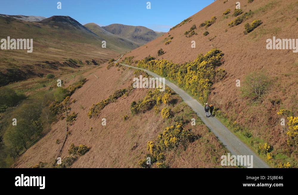 Hikers walking along hillside track on sunny day Coledale Beck in the ...