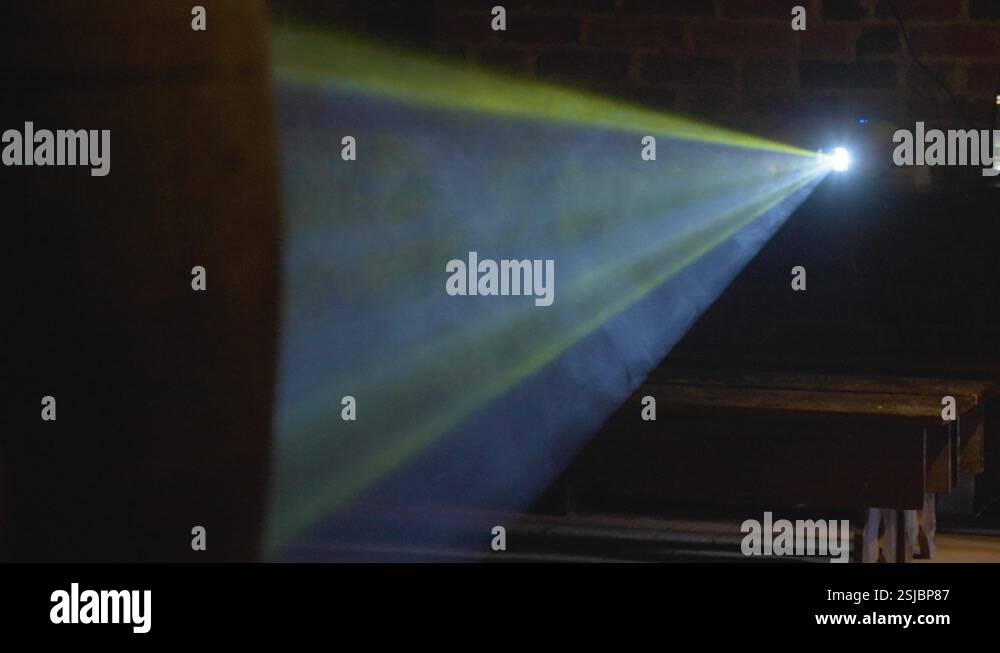 Colourful beams of a projector in an in a dark dramatic room with brick ...