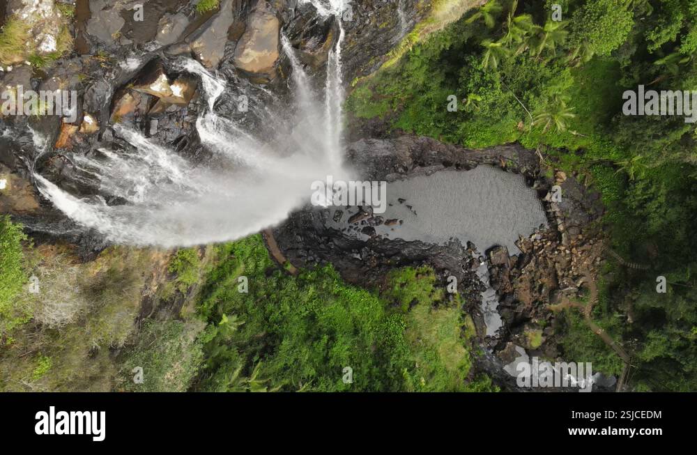 Water cascading over a sheer cliff face into a natural swimming hole ...