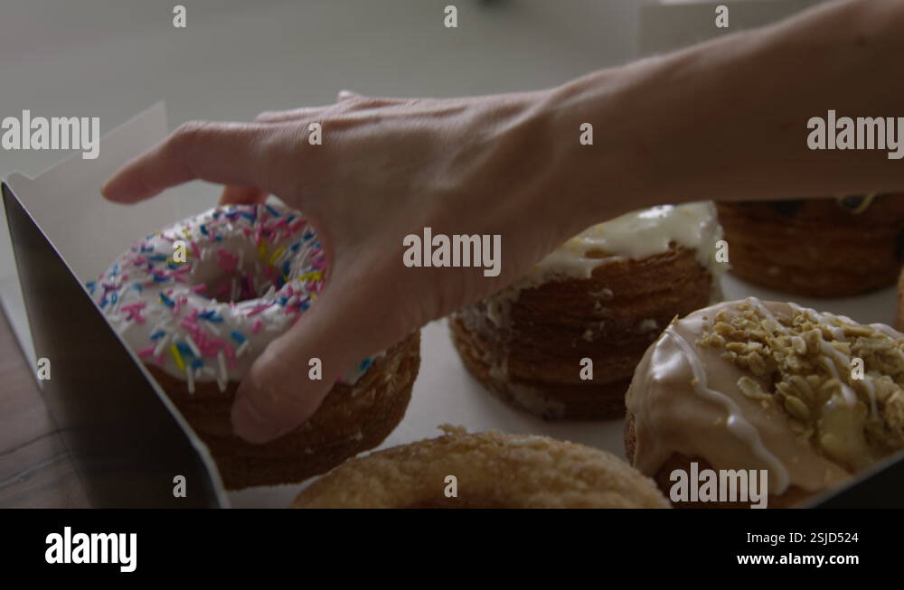 Close up of womans hand reaching in and grabbing a fresh sprinkle donut ...