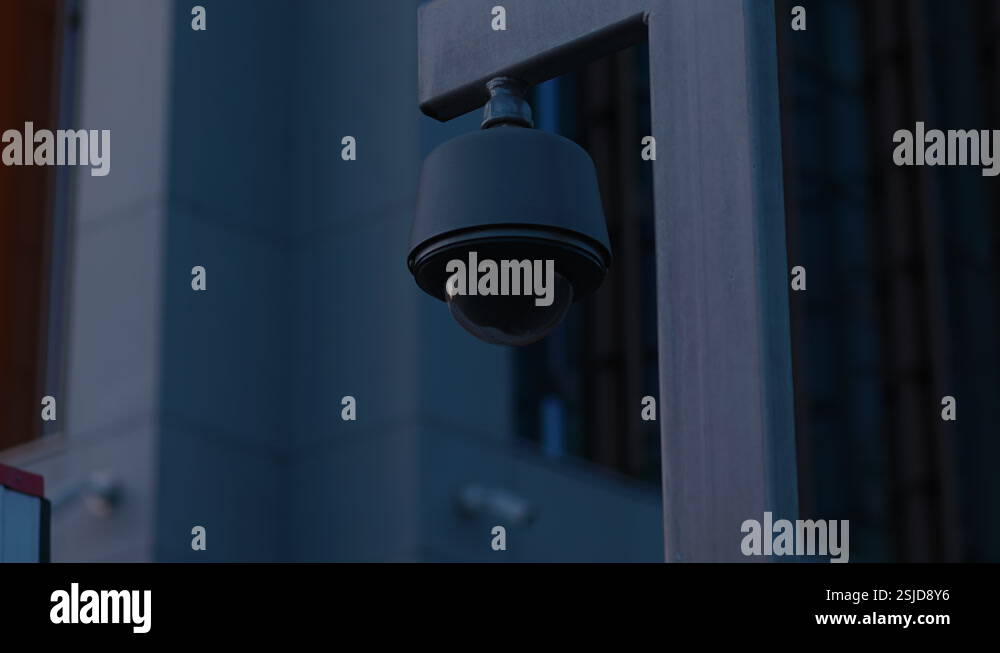 A pole-mounted round black CCTV camera silhouetted against a dark ...