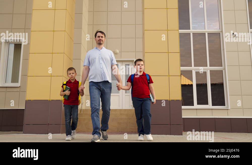 father leads child with backpacks school. two boy sons go school ...