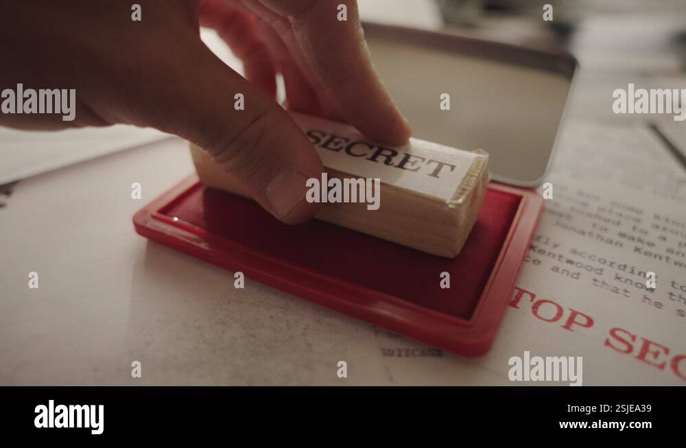 Hand dipping rubber stamp on red ink to mark classified document as Top ...