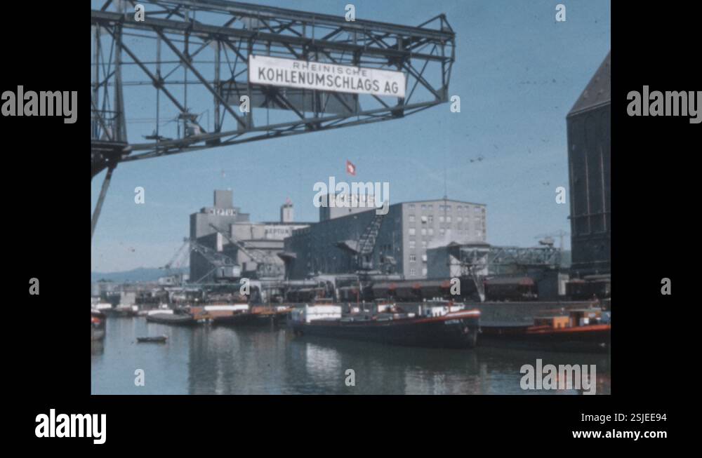 1950s: Barge and warehouses on waterway. Swiss flag flies above Rehenus ...