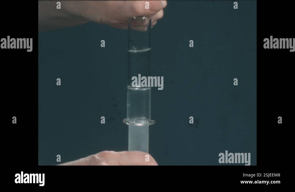 1960s: hands push down on inverted glass graduated cylinder with water ...