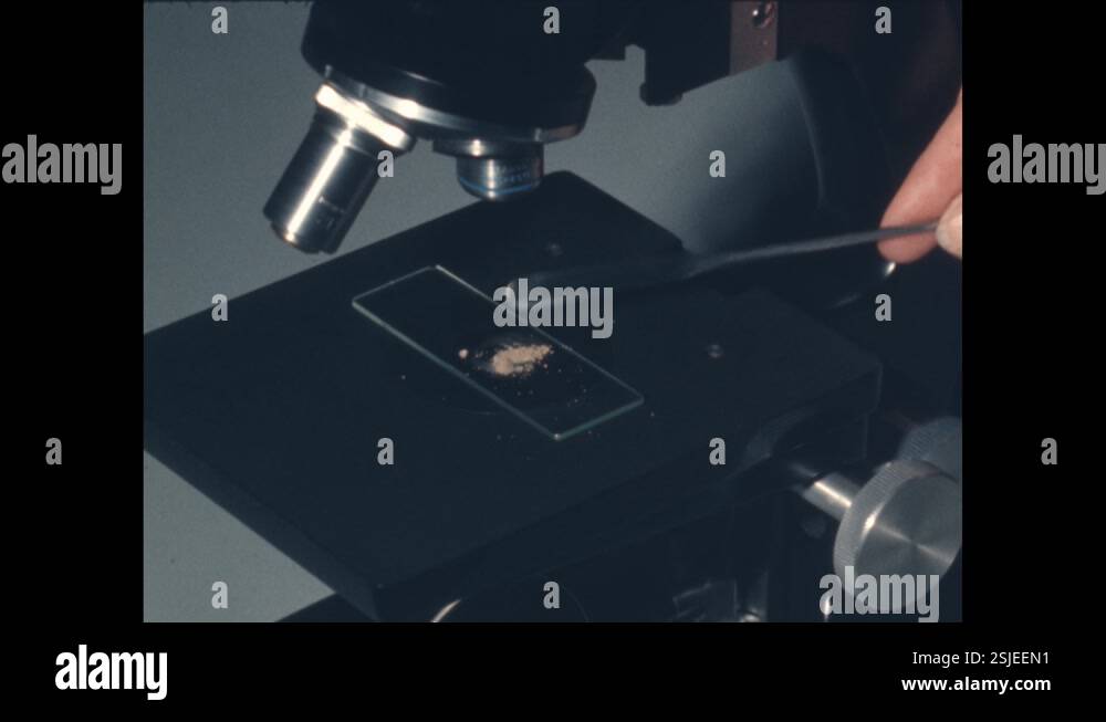 1960s: microscope with glass slide, hand uses thin spatula to dump ...