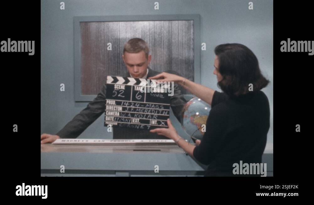 1960s: Slate. Man stands behind a desk with a globe. He puts up signs ...