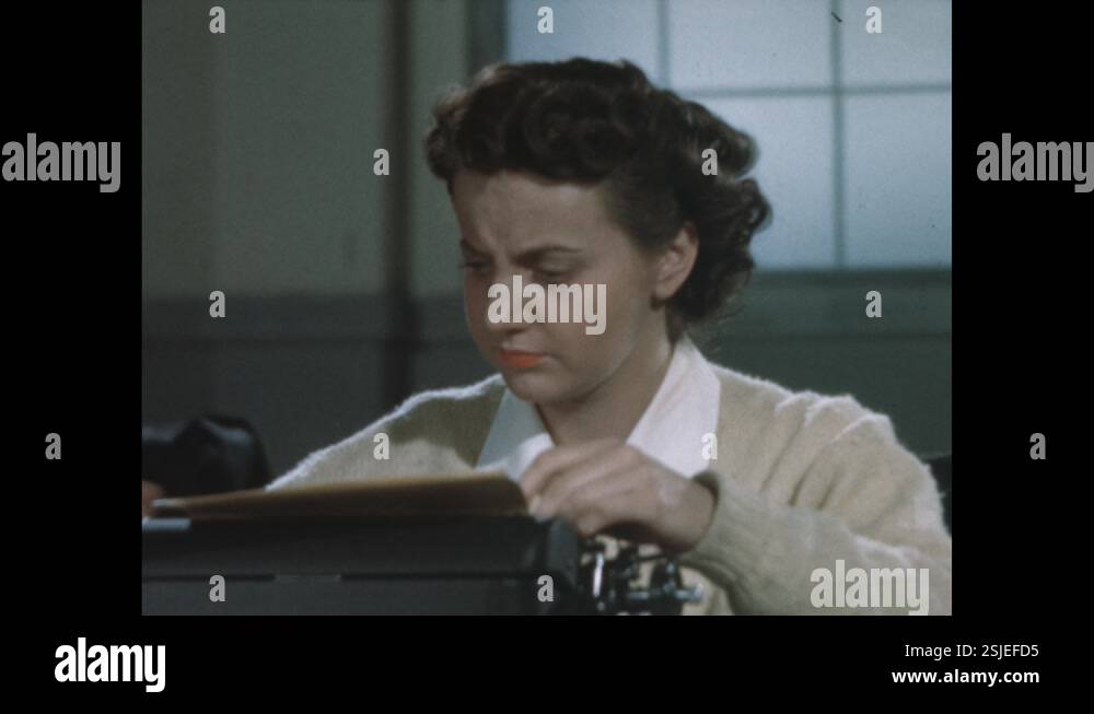 1950s: Teen girl sits down at desk in classroom, rolls paper into ...