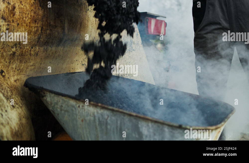 Construction worker loads hot tar into a wheelbarrow from dump truck ...