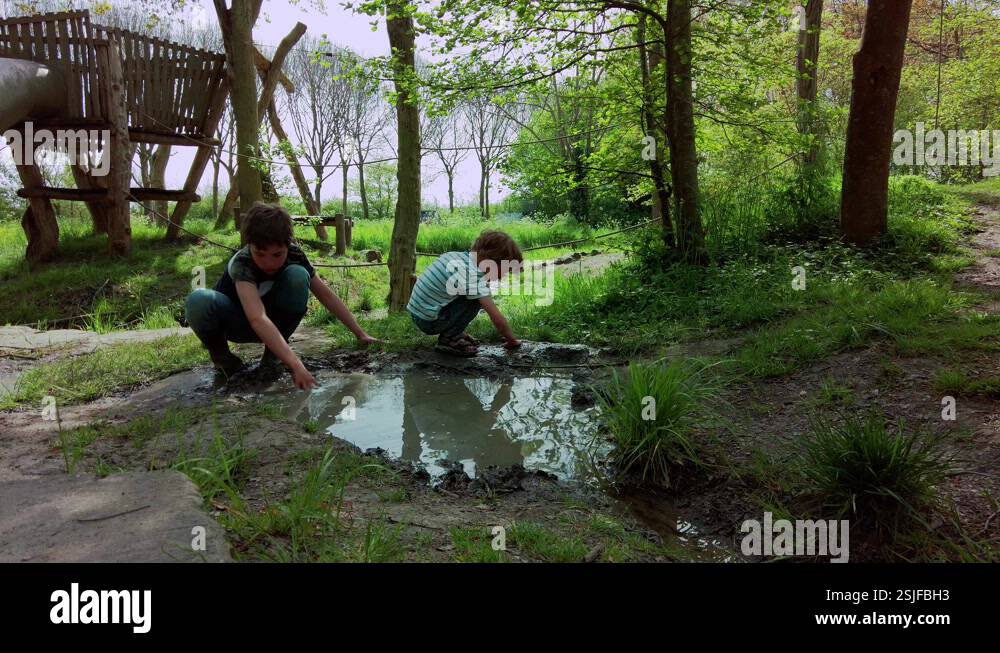 Two boys play with mud and water in a puddle in the shade Stock Video ...