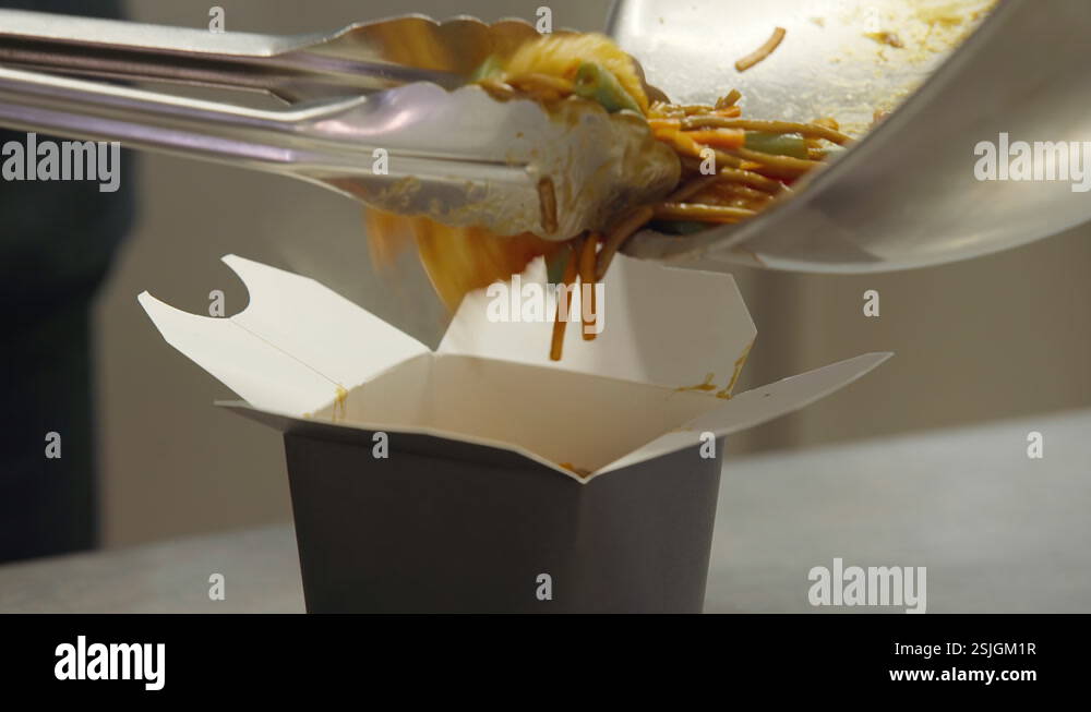 Using tongs to place tasty chinese cuisine food inside of the box ...