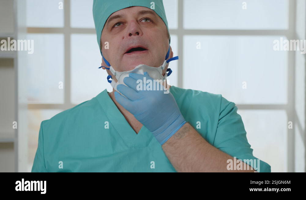 Tired male doctor surgeon takes off protective mask respirator from his ...