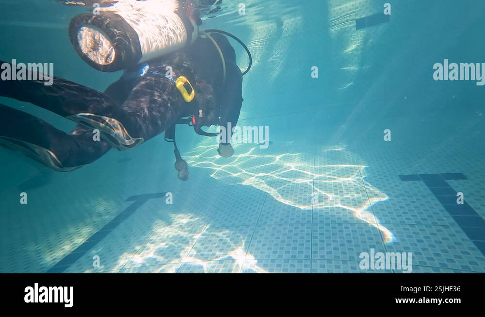 Man in a pool wearing scuba gear, he swims away and then turns around ...