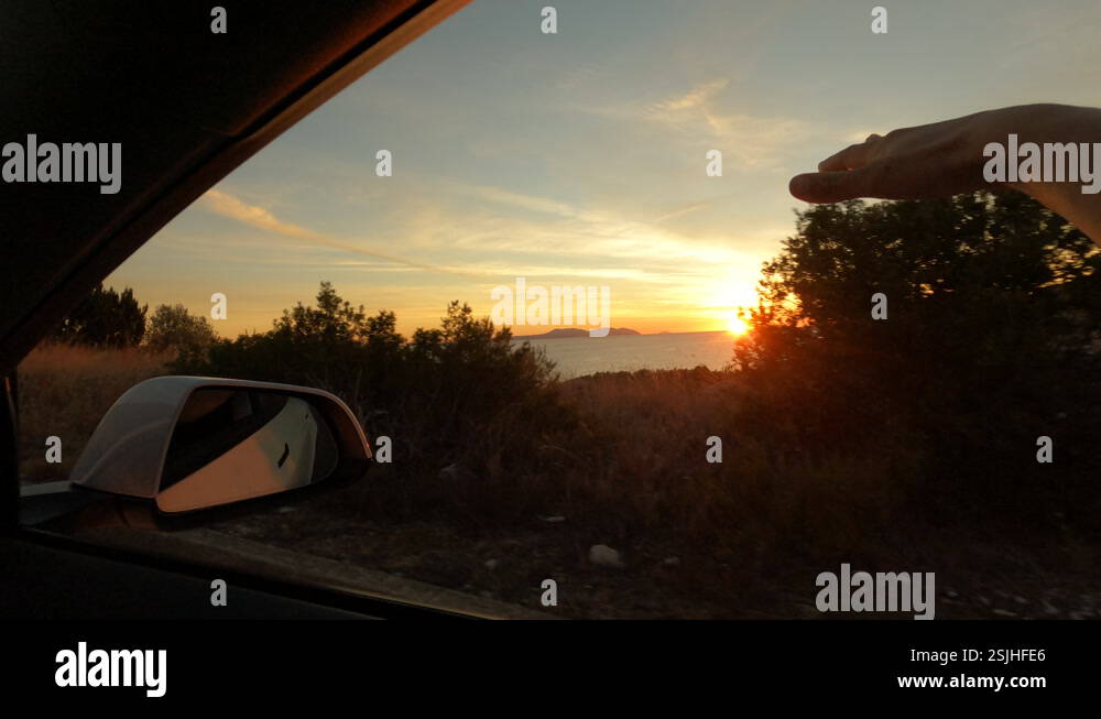 LENS FLARE: Woman's hand waves through window of car driving along the ...
