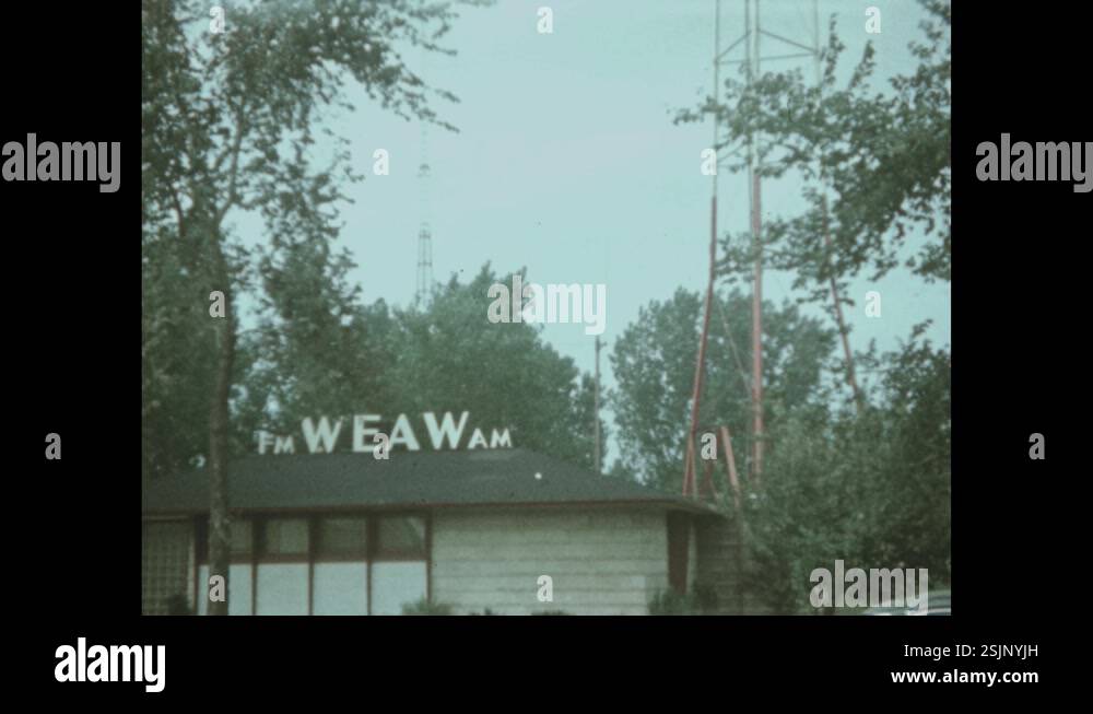 1950s: DJ turns knobs on control panel at radio station. Sign and tower ...