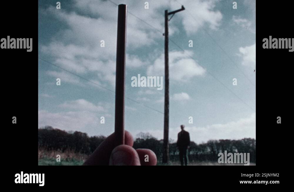 1970s: Man poses near telephone pole and handheld stick. Hand lifts and ...