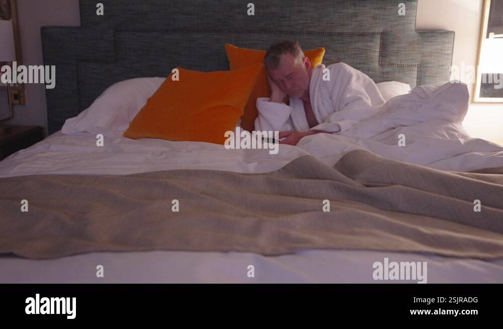 Man lying in bed at night wearing dressing gown and texting on his ...