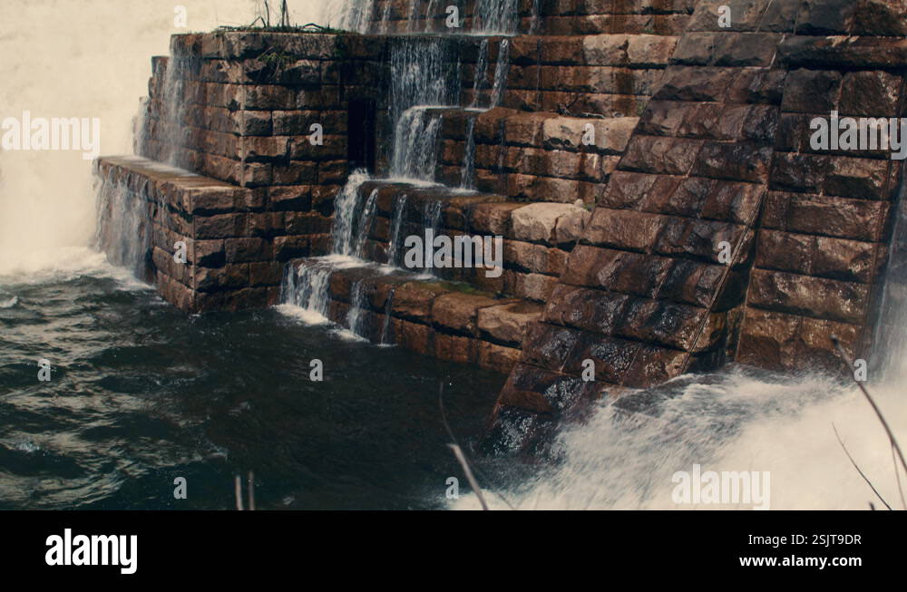water falling down stepped spillway around small tree at the bottom of ...