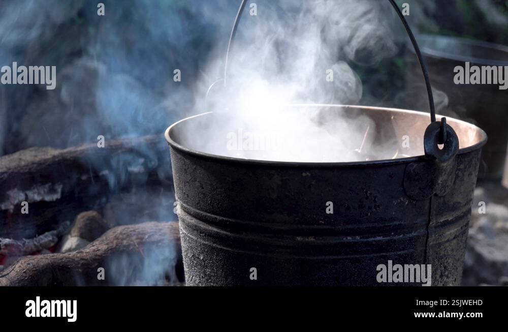 Boiling water in metal bucket on a smoldering bonfire at a forest ...
