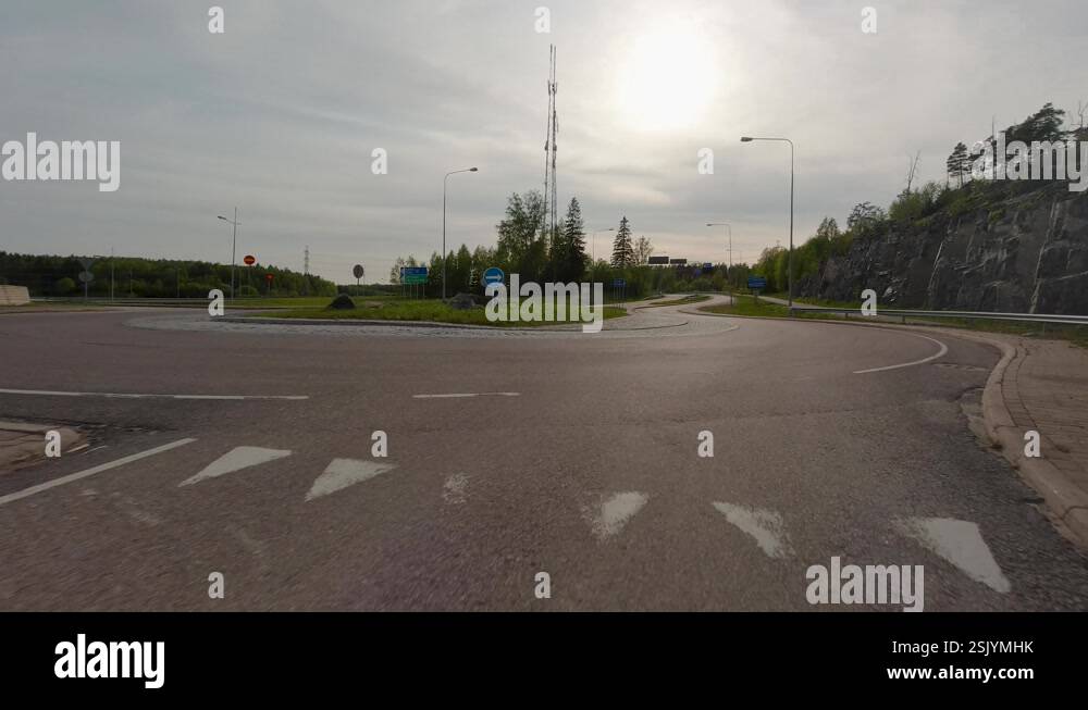 Cars drive along the road with green grass, trees, and road signs. The ...