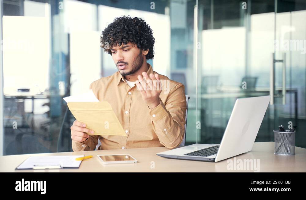 Disappointed young employee reading letter with bad news while sitting ...