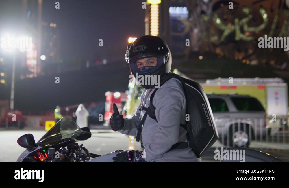 A man on a motorcycle signing a thumbs up. The man is wearing a black ...