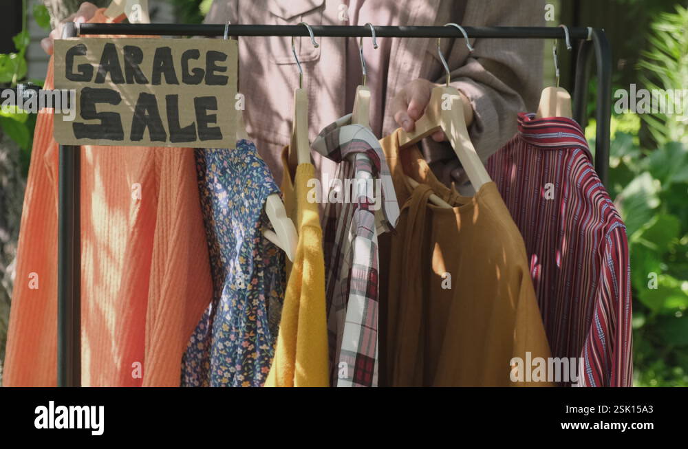 Garage sale. Person browsing through clothes hanging on rack at garage ...
