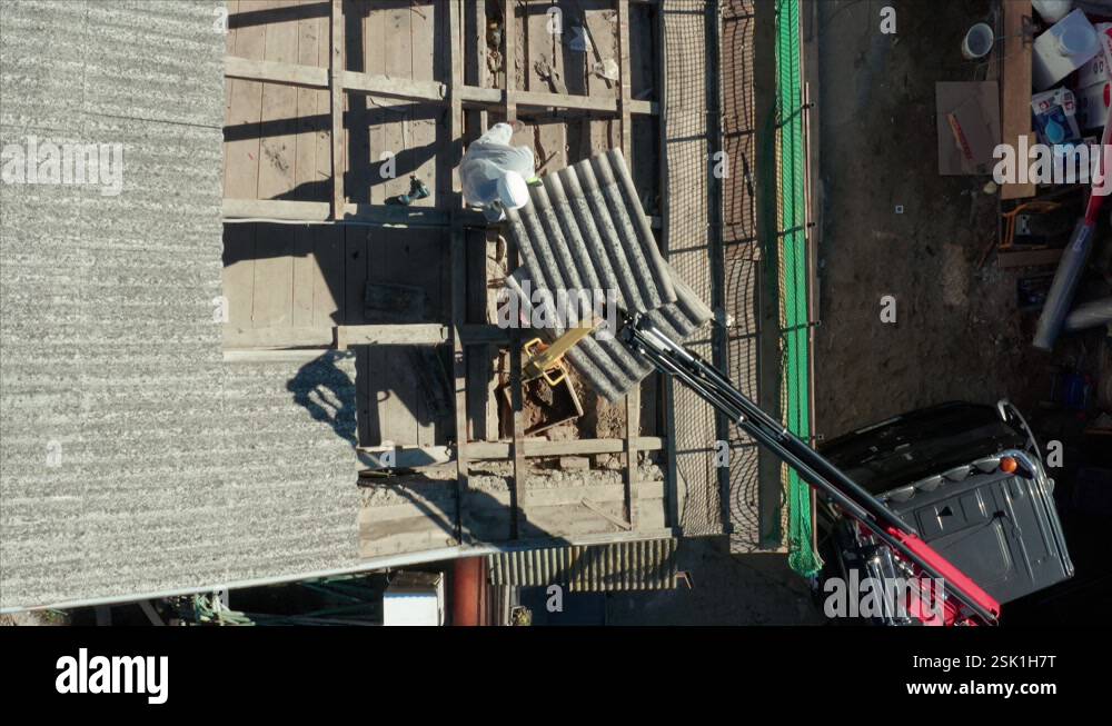 Overhead aerial of worker and crane fixing metal roof on wooden house ...