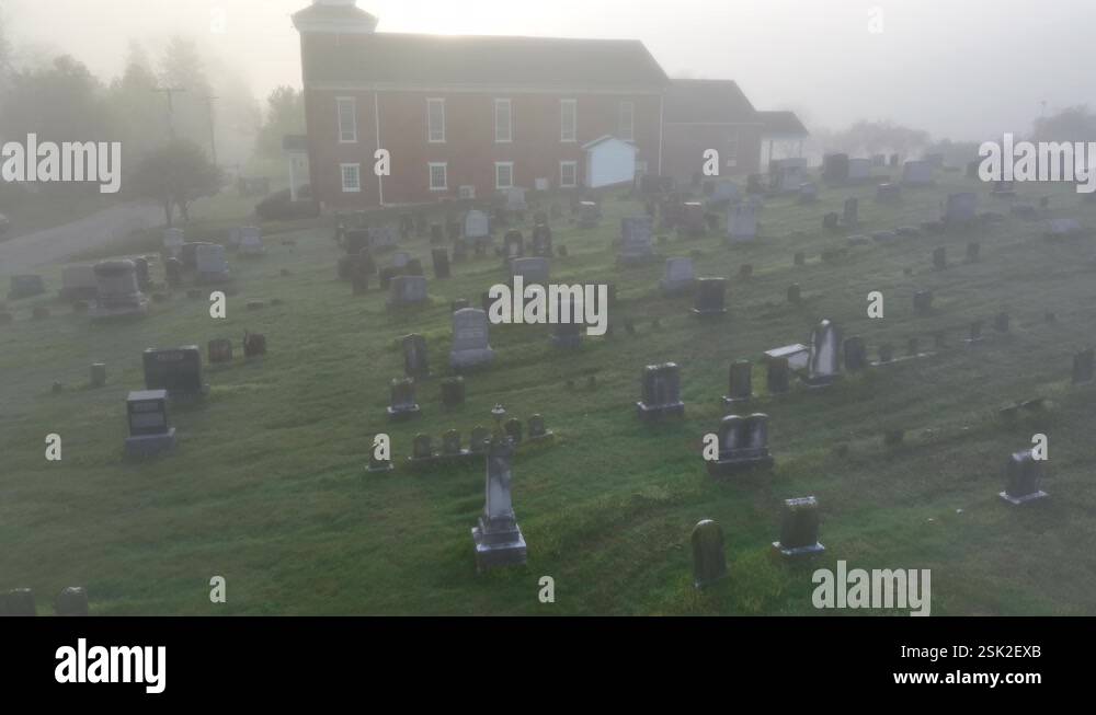 Old graveyard in front of red church engulfed in eerie fog, aerial ...