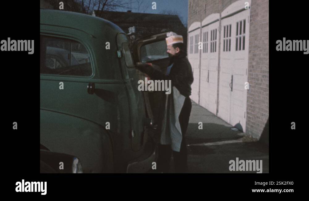 1950s: Man in butcher's cap and apron carries a basket out to a van ...