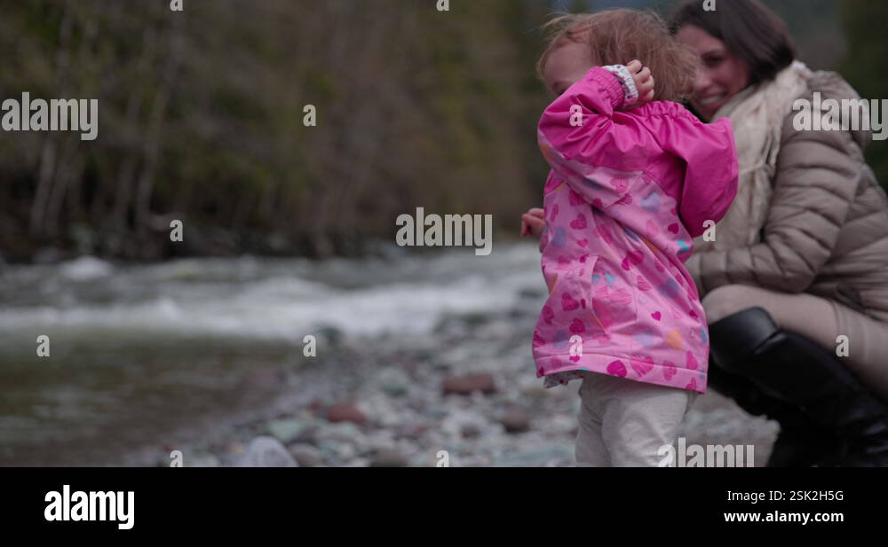 Toddler girl throwing rocks into river at base of mountain - side ...