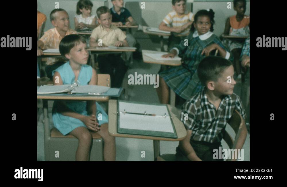 1960s: Students sit in classroom desks, listening. Young girl raises ...
