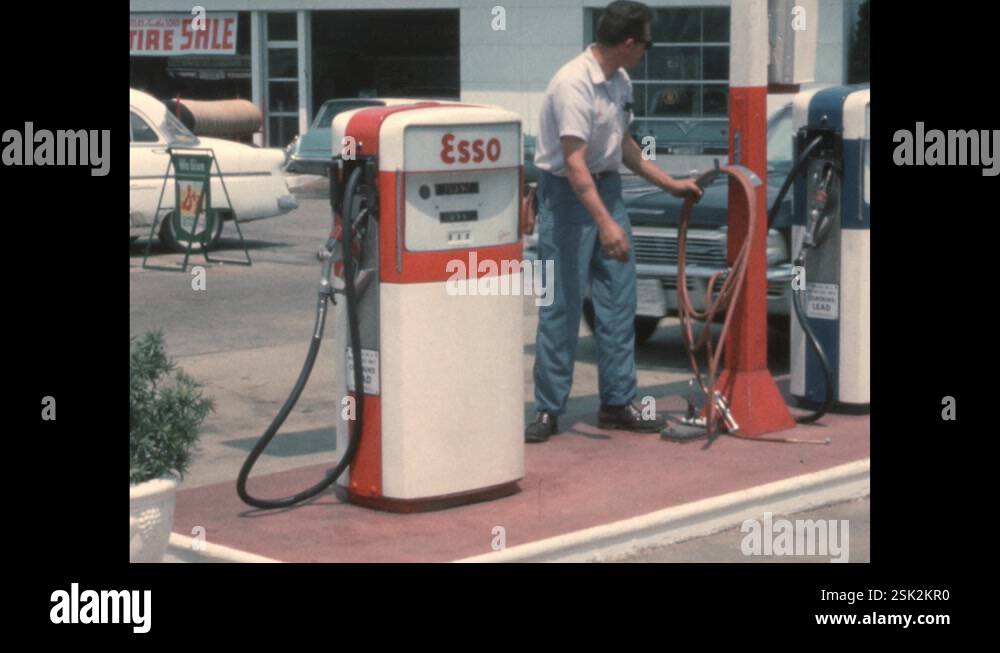 1960s: Woman drives station wagon up to man at gas pumps in service ...