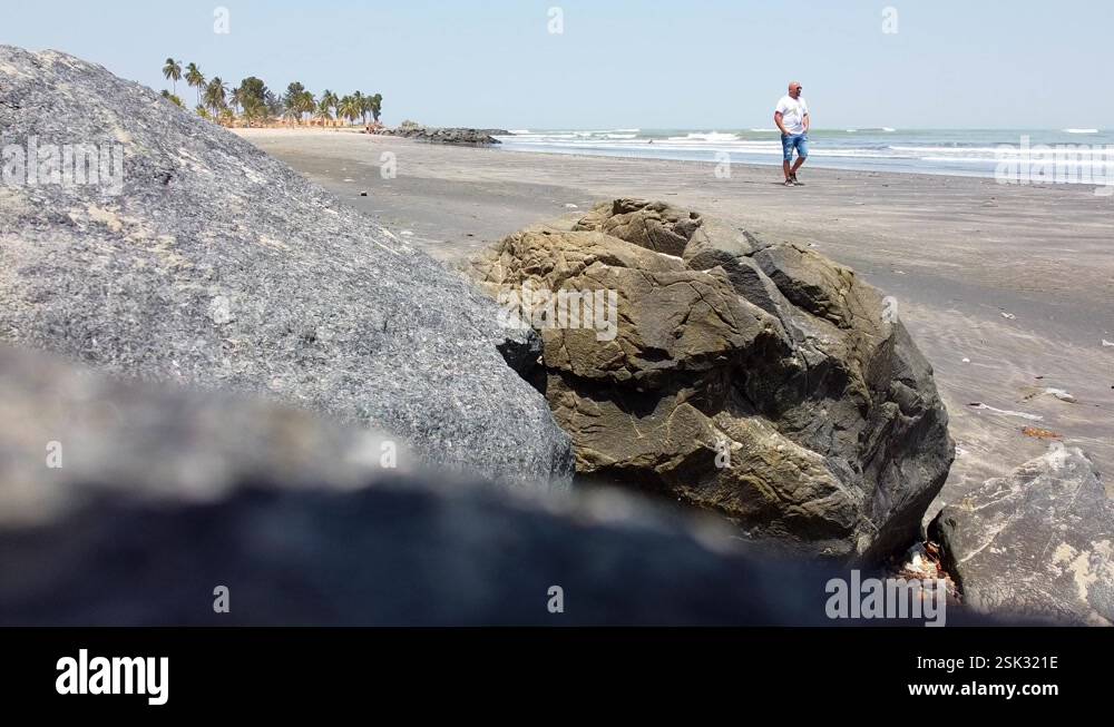static shot of a man walking on beach in Africa with rocks in the Stock ...
