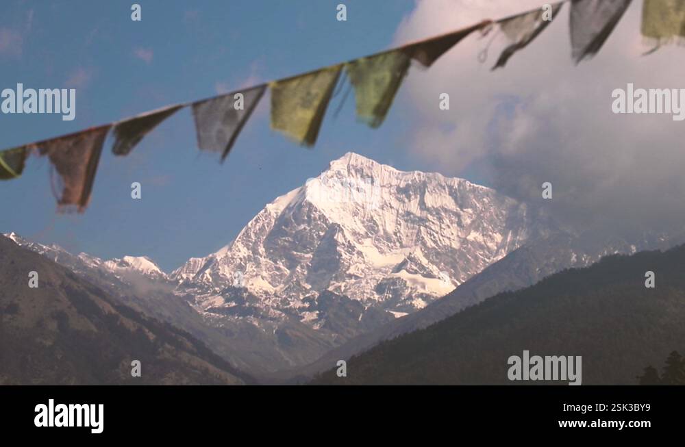 close up of Nepali prayer flags in first plane and a big snowy mountain ...