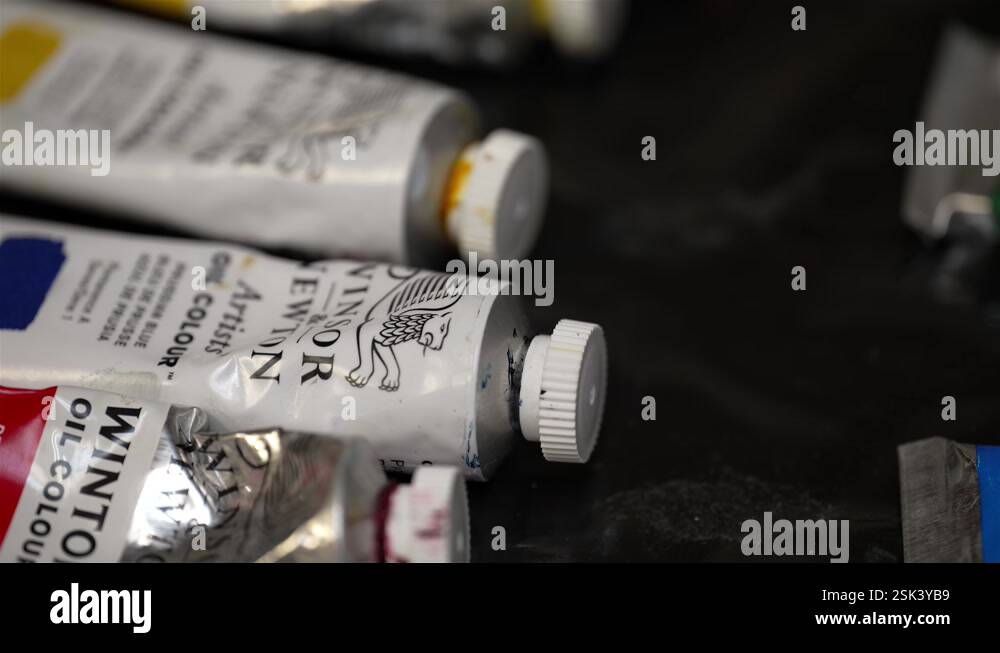 Narrow depth of field pan down along tubes of oil paint on black desk ...