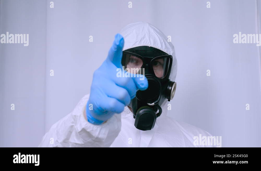 Man in a chemical protective suit with a gas mask pointing with his ...