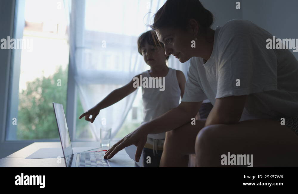 Mother multi tasking working from home in front of laptop computer with ...