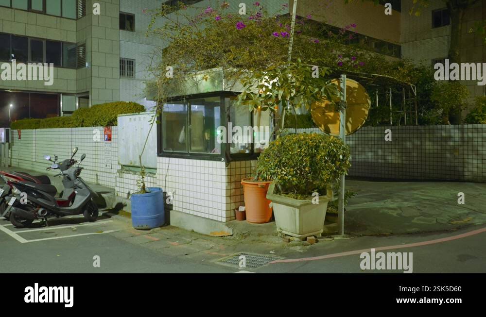 Security guard shack covered in plants next to parked mopeds at night ...